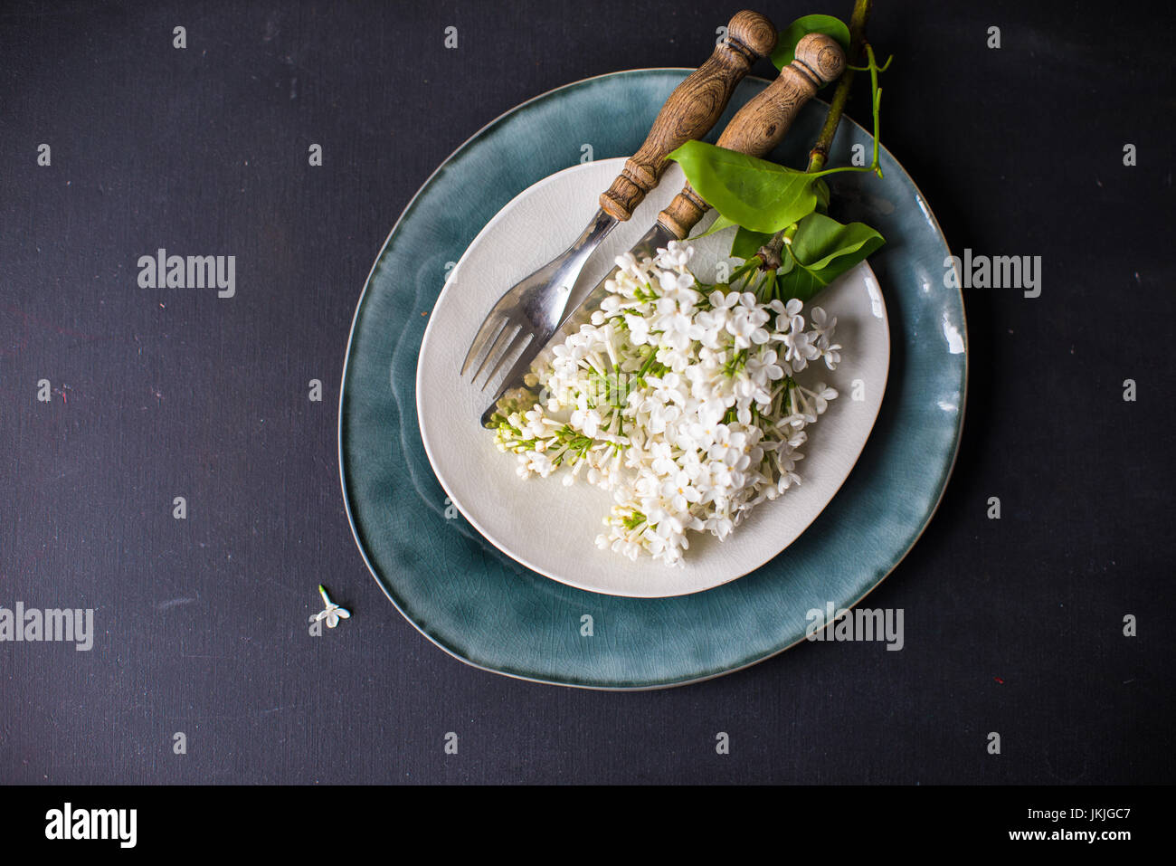 Pring Table Setting With White Lilac Flowers On The Plate With Flatware On Rustic Wooden Table