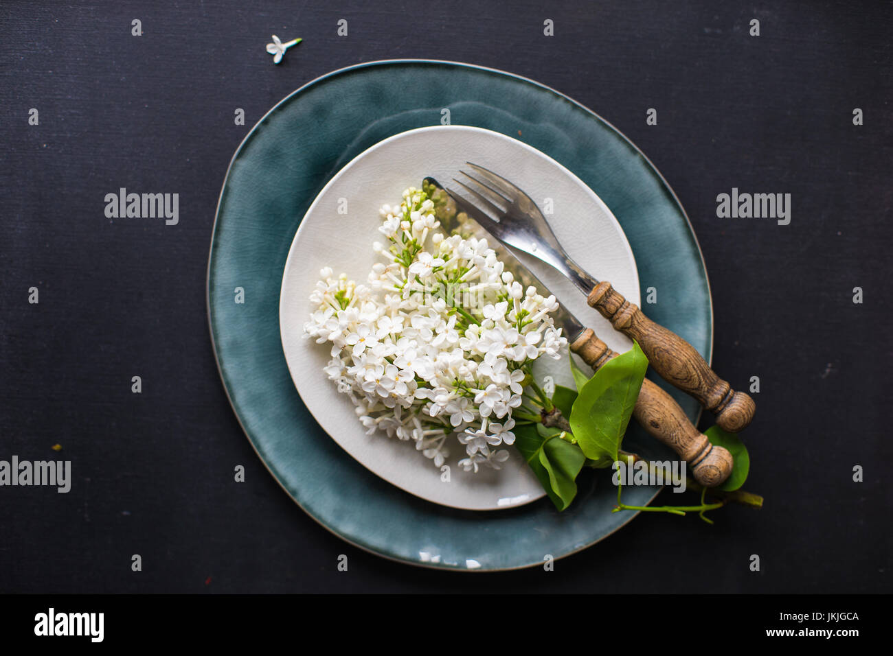Pring Table Setting With White Lilac Flowers On The Plate With Flatware On Rustic Wooden Table