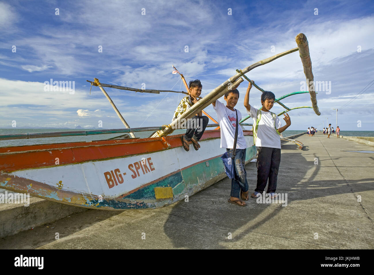 Three Filipino schoolboys hang out on the pontoon of an outrigger canoe ...