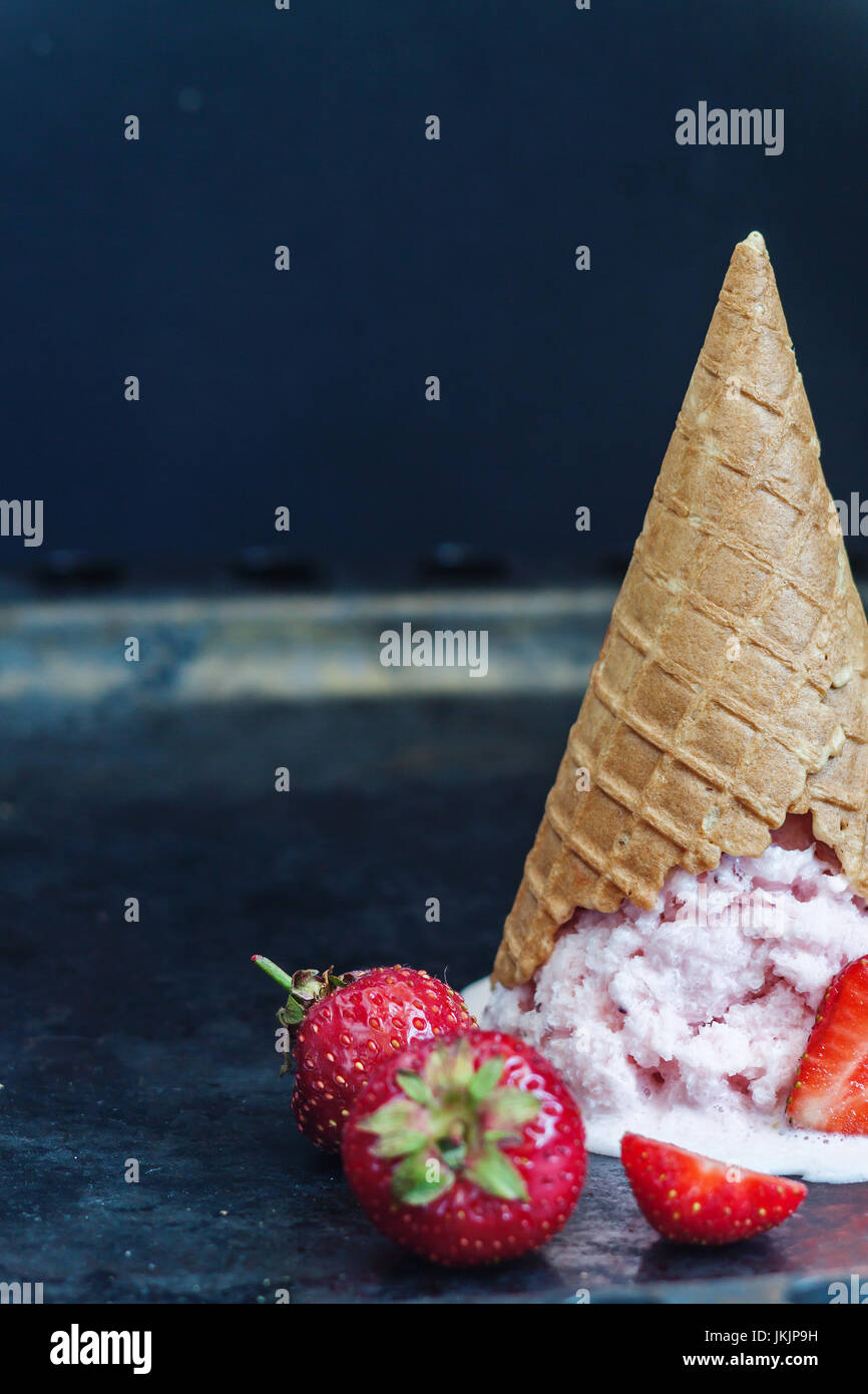Strawberry ice cream in a waffle cone inverted and melted against a ...