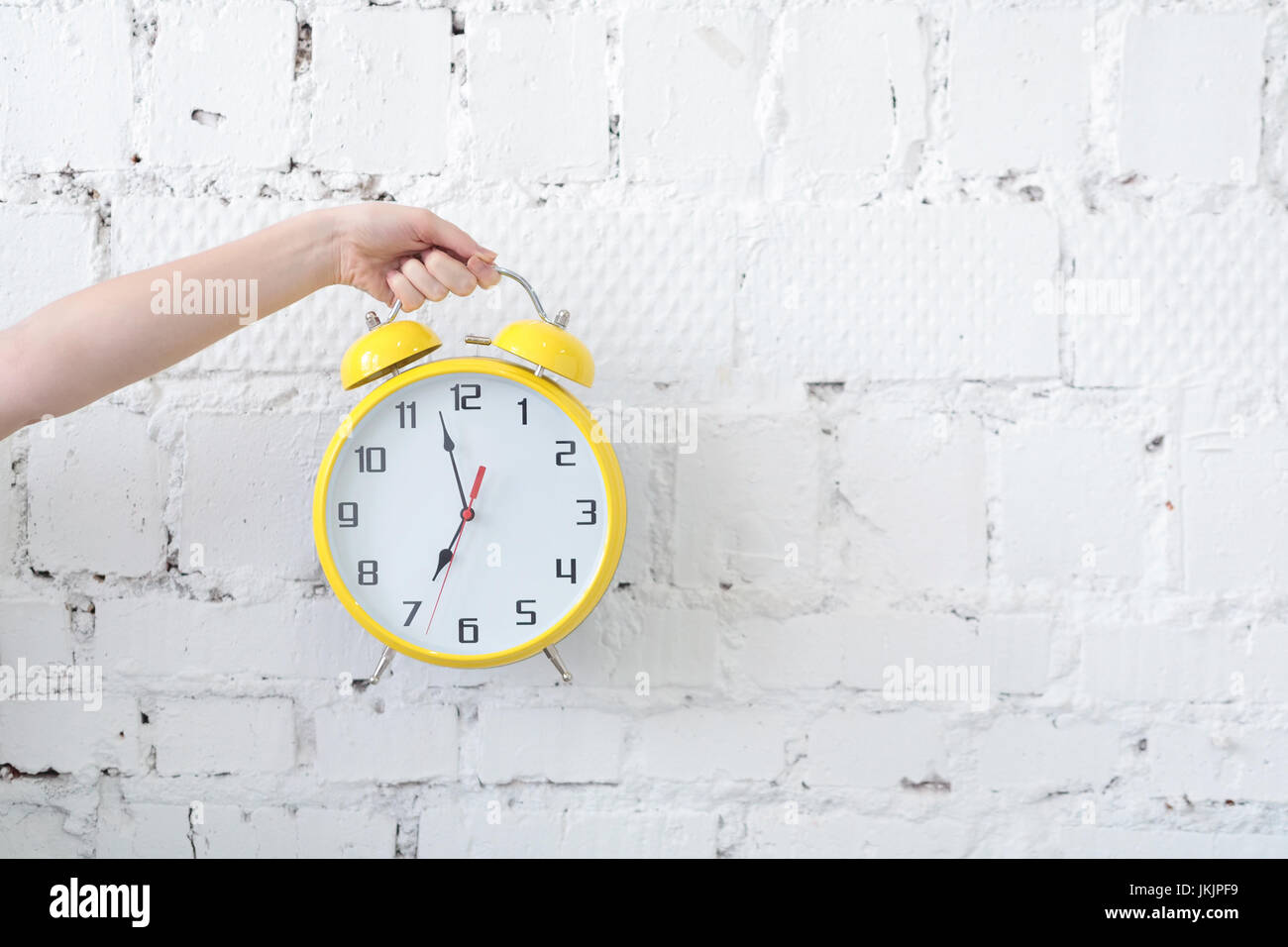 Hand holding alarm clock against white brick wall Stock Photo - Alamy
