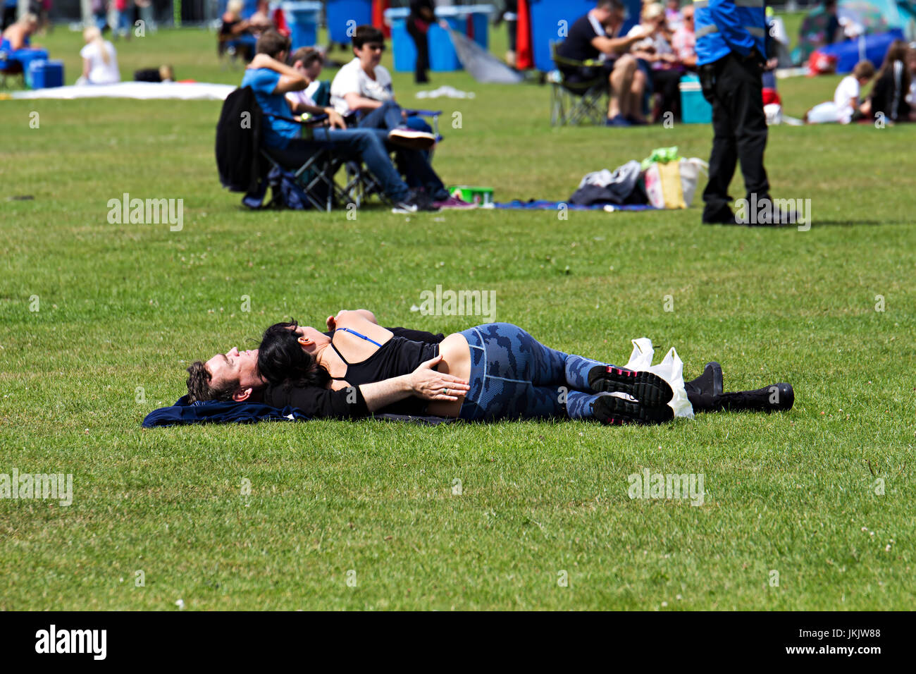 Young couple having a cuddle on the grass at an outdoor music festival ...