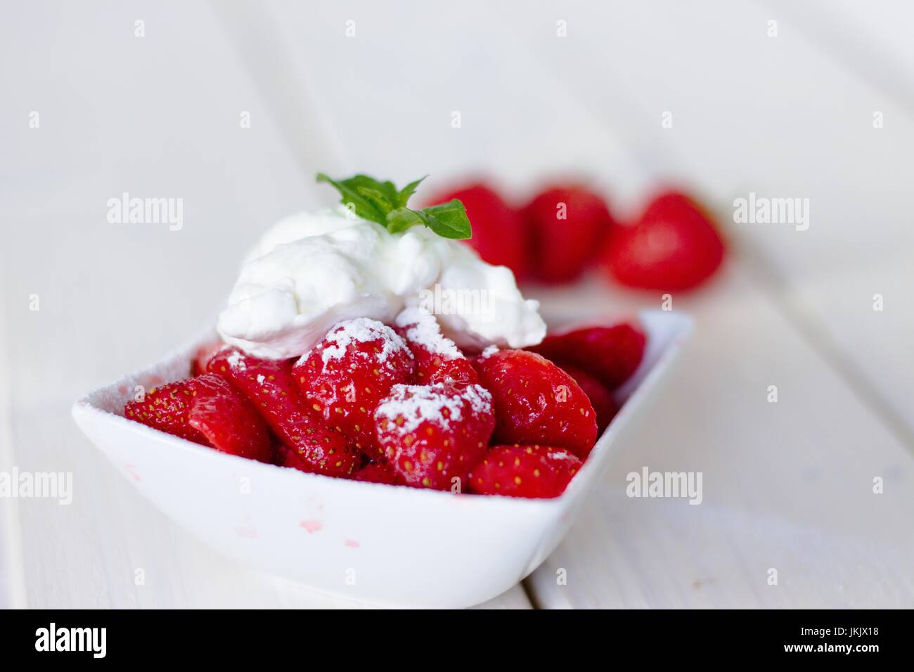 Square shaped bowl of strawberries with sugar, whipped cream and mint ...
