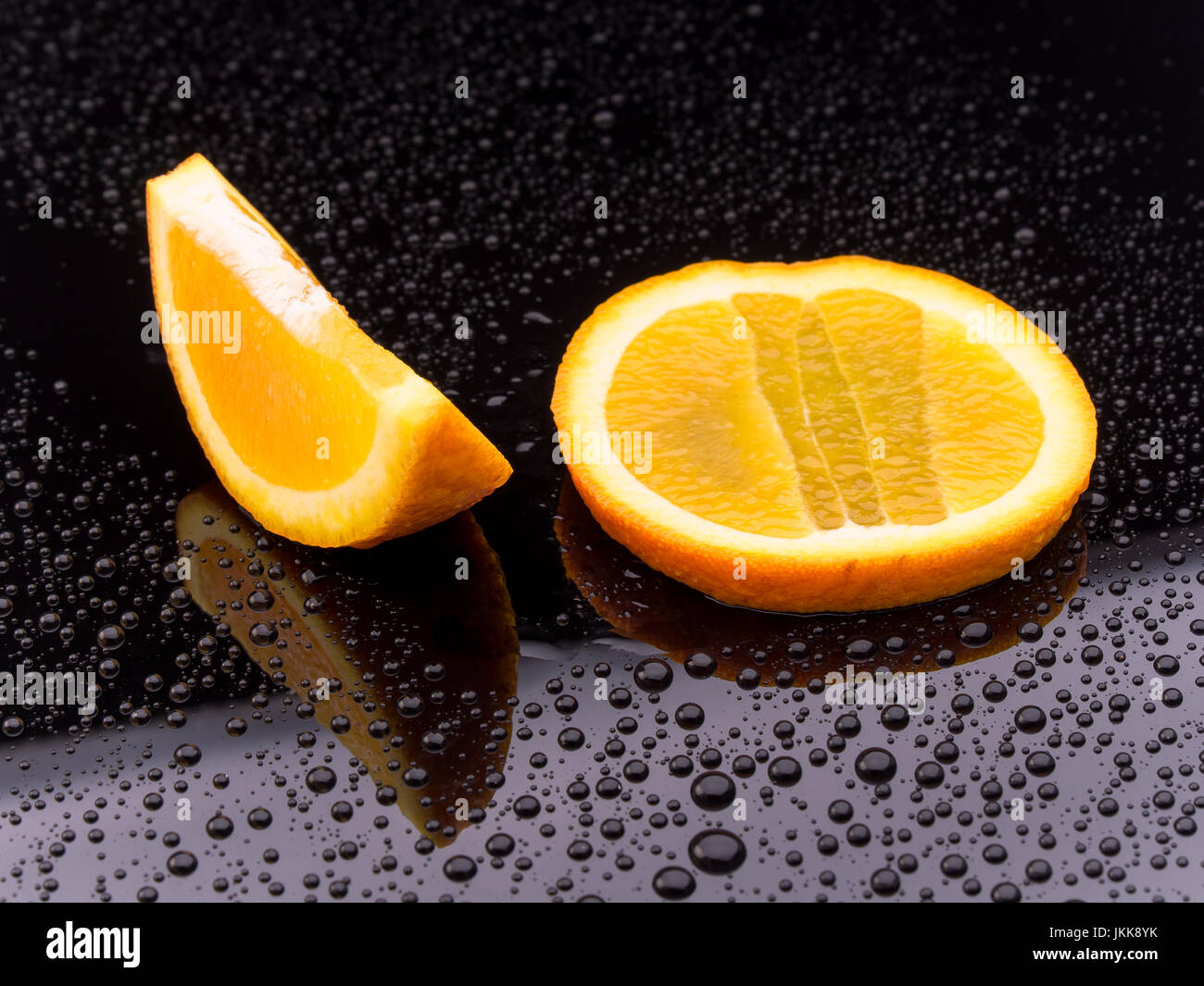 Healthy orange fruit slices on a black surface with reflection and ...