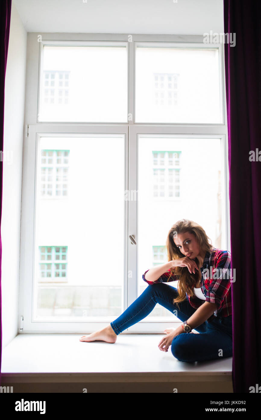 Beautiful woman looking through window while sitting at windowsill at ...