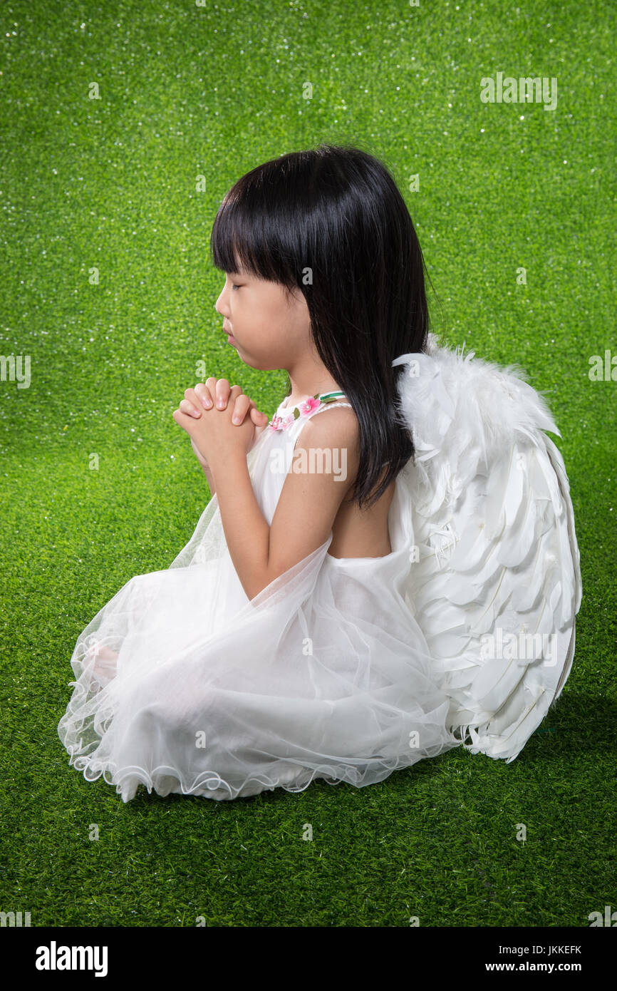 Asian Chinese little girl wearing angel wings and praying at outdoor ...
