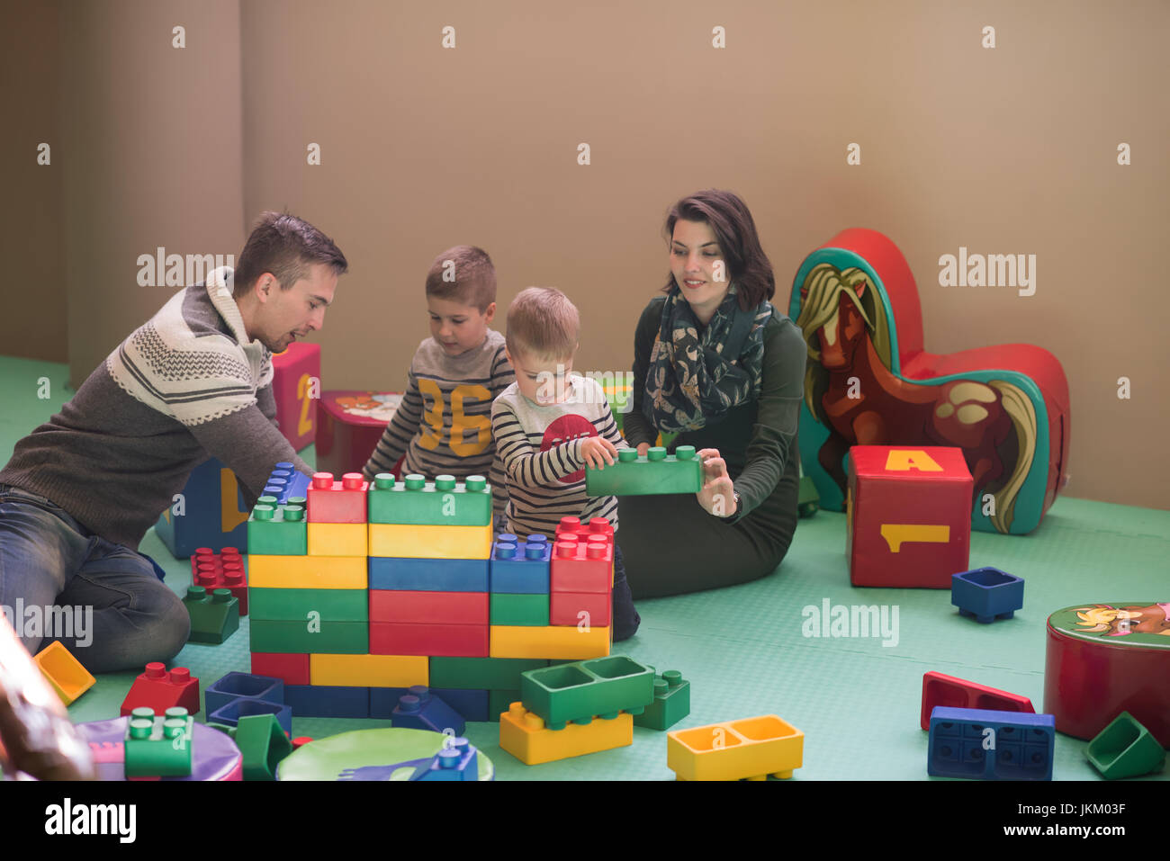 young happy parents having fun with kids in children playground indoor ...