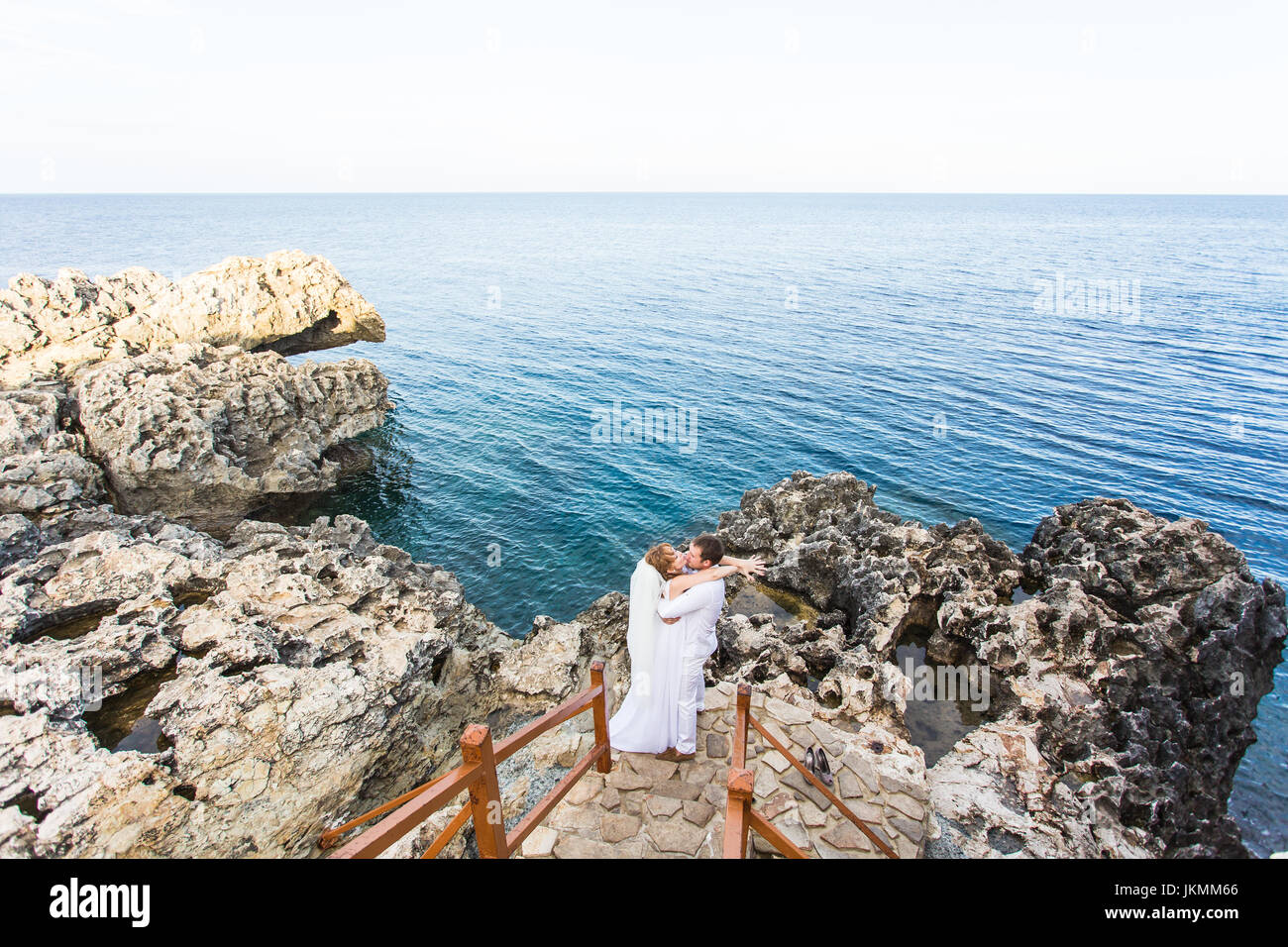 Couple in love young bride and groom dressed in white hugging on cliff ...