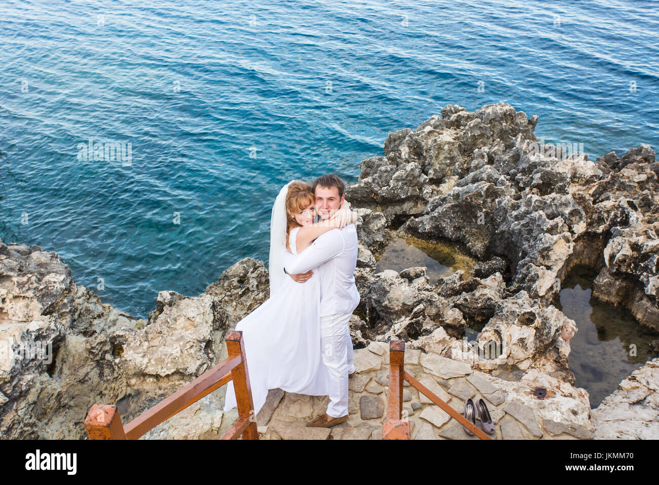 Couple in love young bride and groom dressed in white hugging on cliff ...