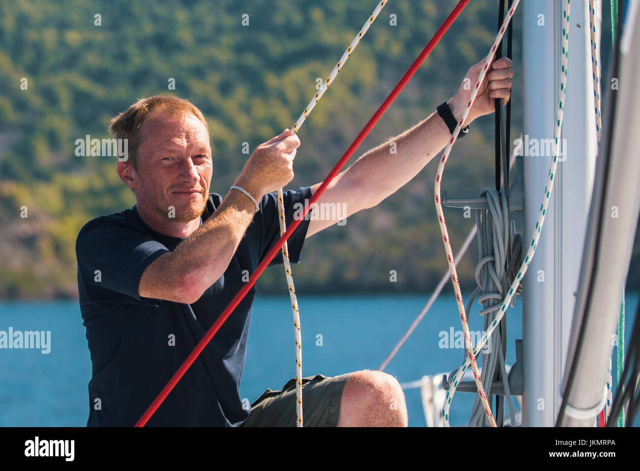 Young man tightens the ropes on the sails of the yacht. Sailing and ...