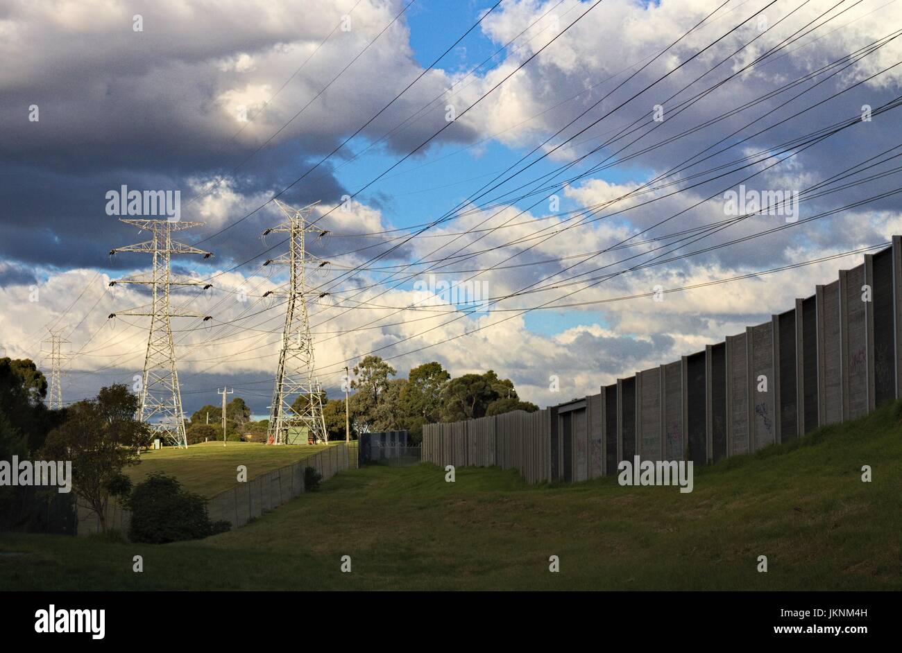 View of high tension power lines over a low green hill with a freeway ...
