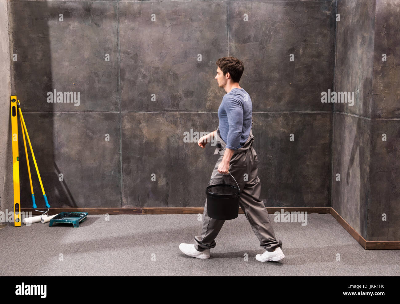 Side view of young laborer walking with paint bucket indoors ...