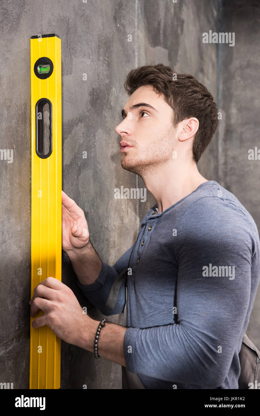 Professional young worker measuring wall with level tool, renovation ...