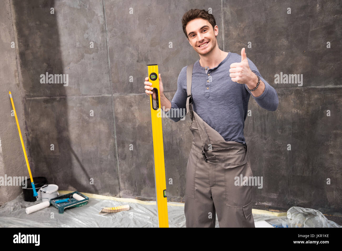Handsome young worker leaning on level tool and looking at camera ...