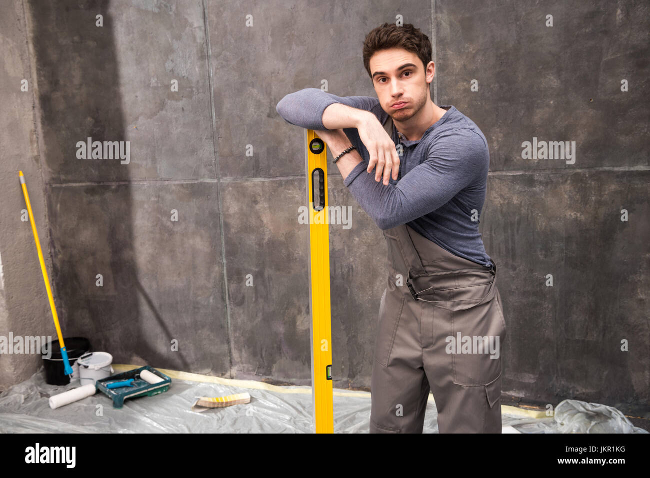 Handsome young worker leaning on level tool and looking at camera ...