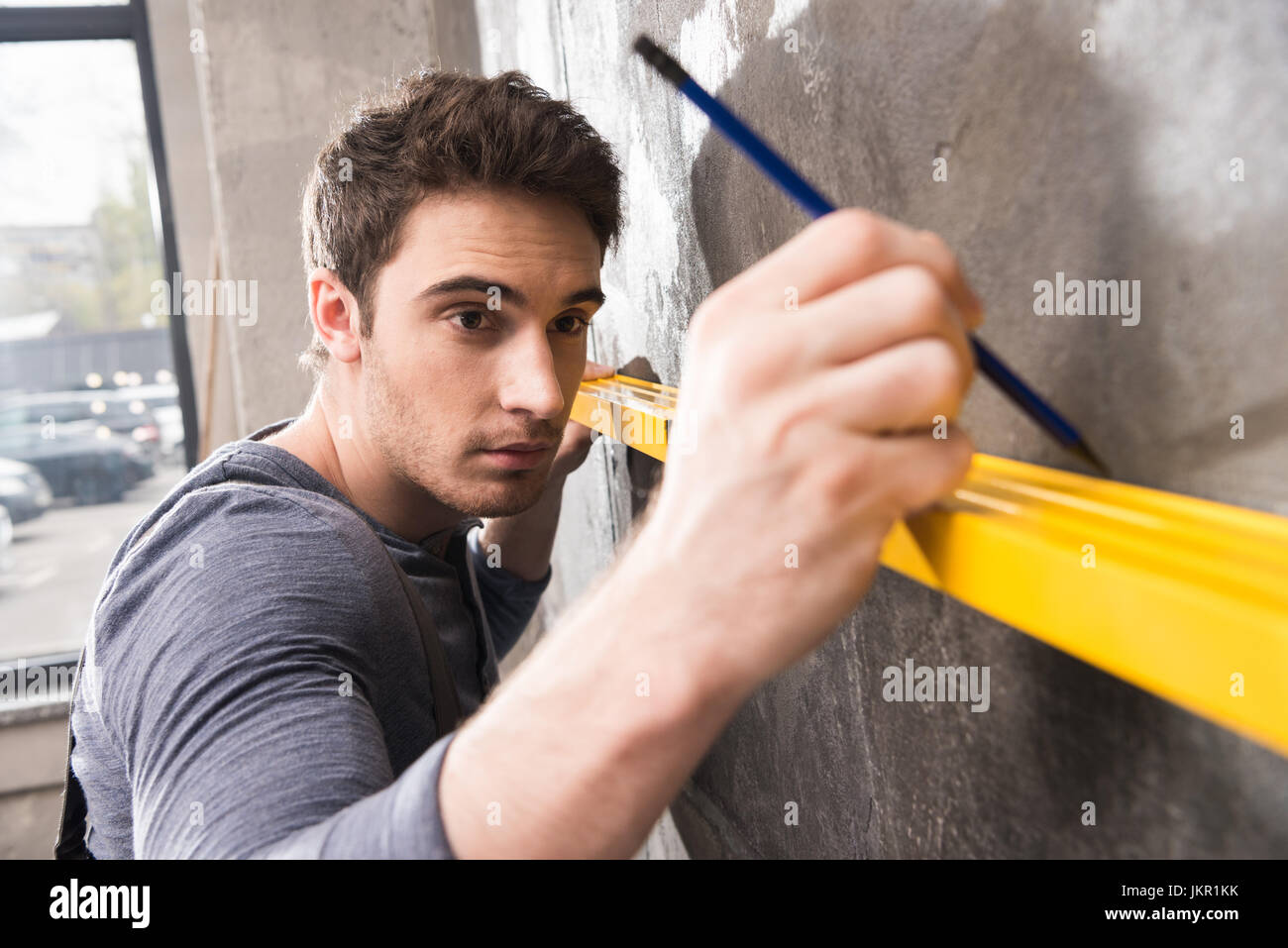 Handsome young laborer with pencil measuring wall with level tool ...