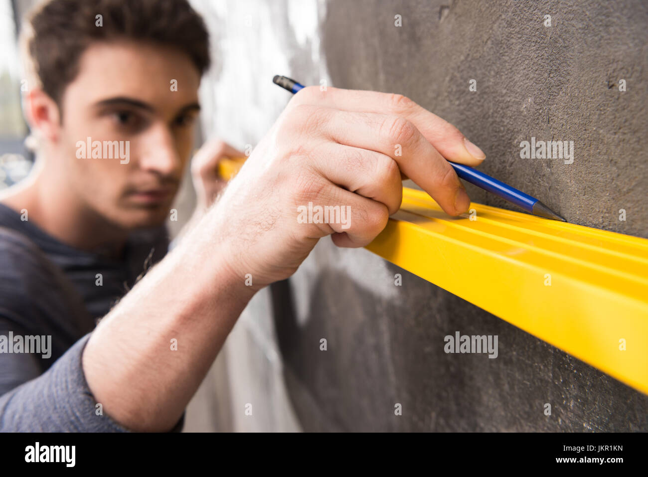 Handsome young laborer with pencil measuring wall with level tool ...