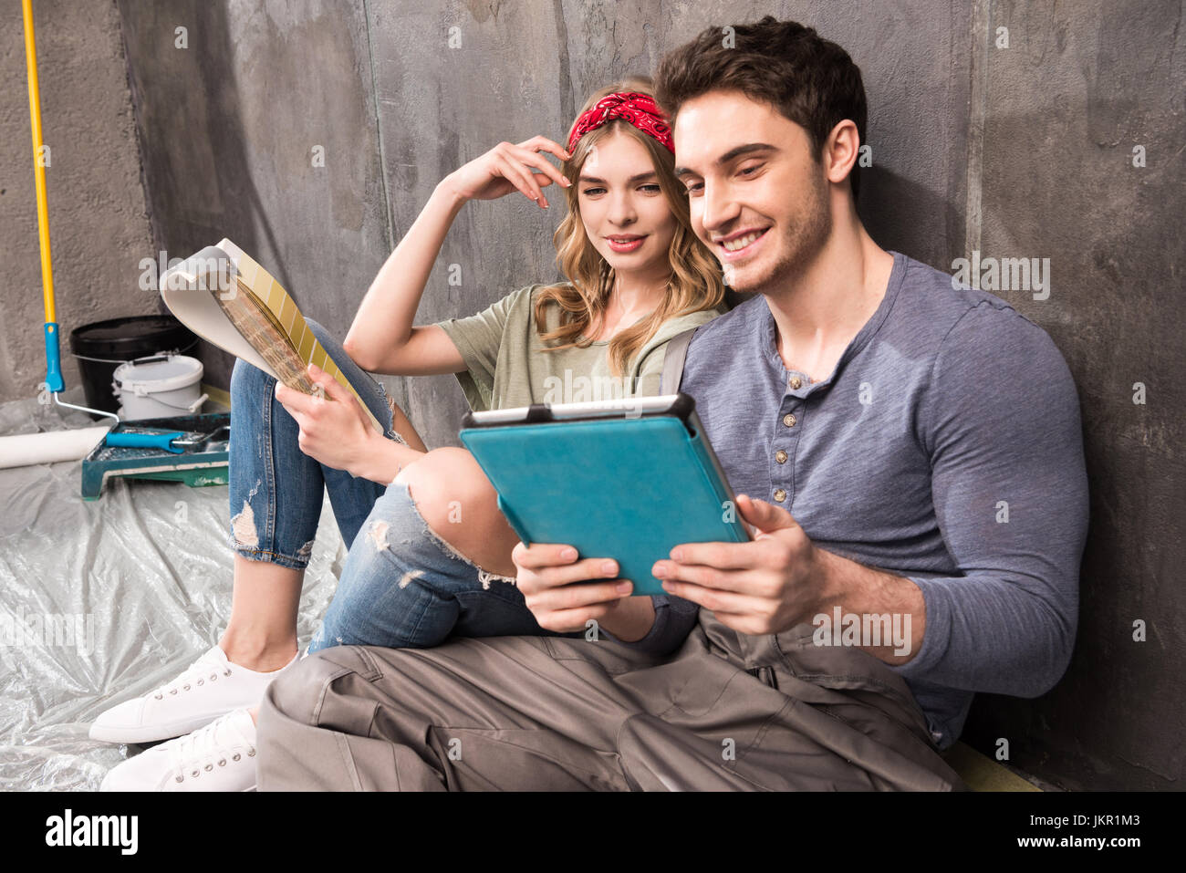 Smiling young couple sitting on floor with digital tablet and choosing samples for renovation ...