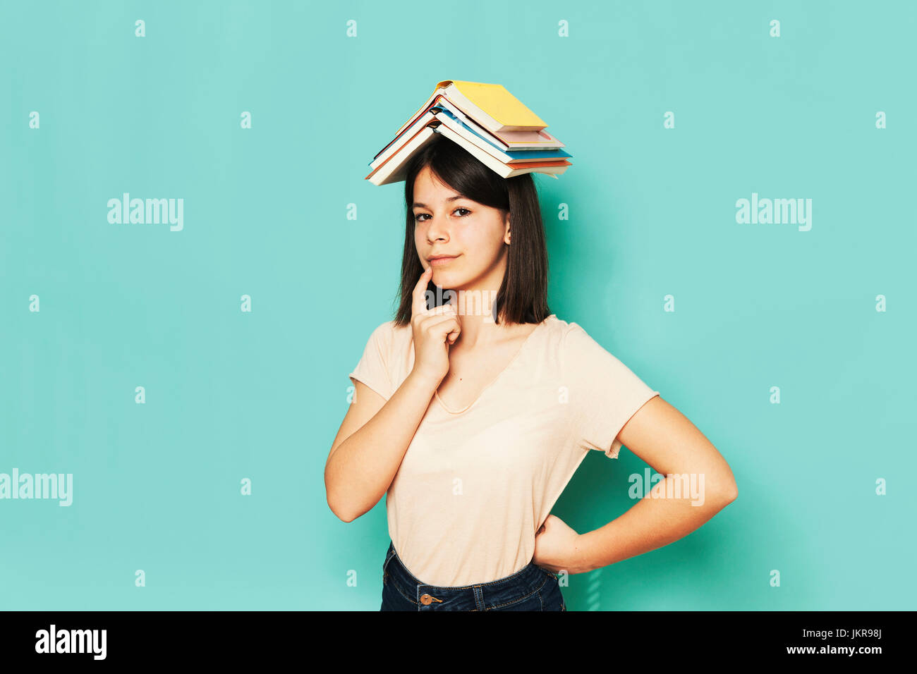 Portrait of girl balancing book against turquoise background Stock ...