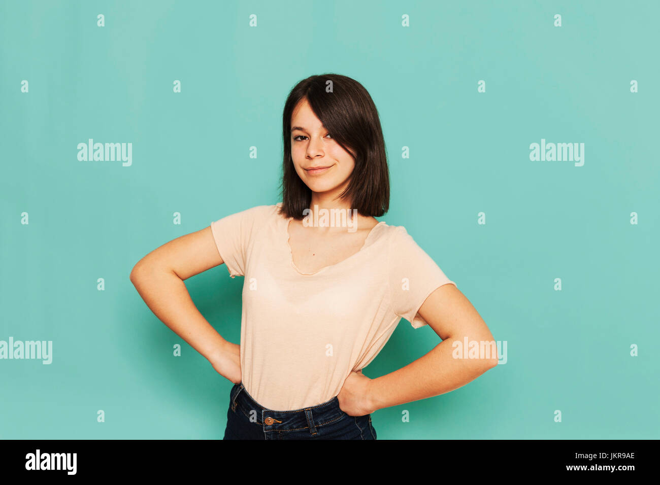 Portrait of confident girl standing with hands on hip against turquoise ...