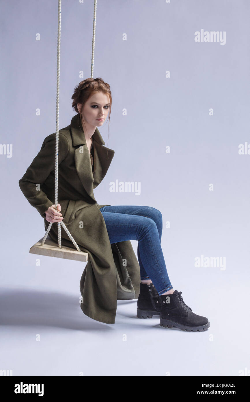 Full length of woman wearing long coat sitting on swing against purple ...
