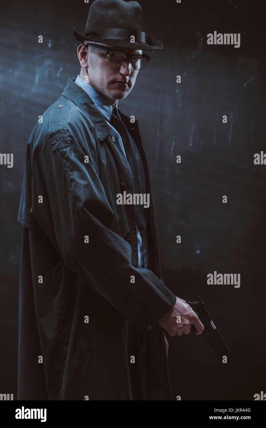 Portrait of confident man holding gun standing against black wall Stock ...