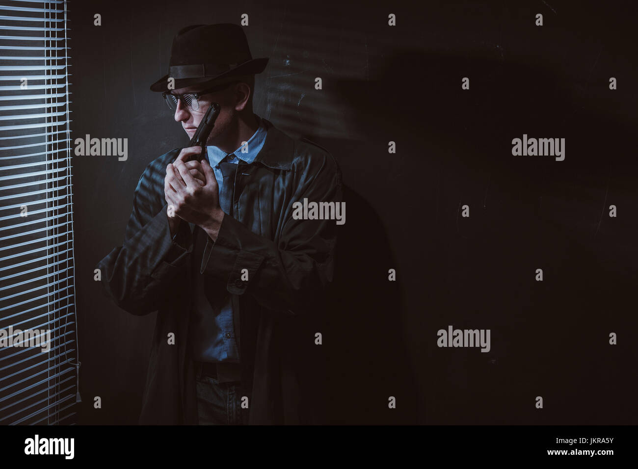 Young man standing with gun by window against black wall Stock Photo ...