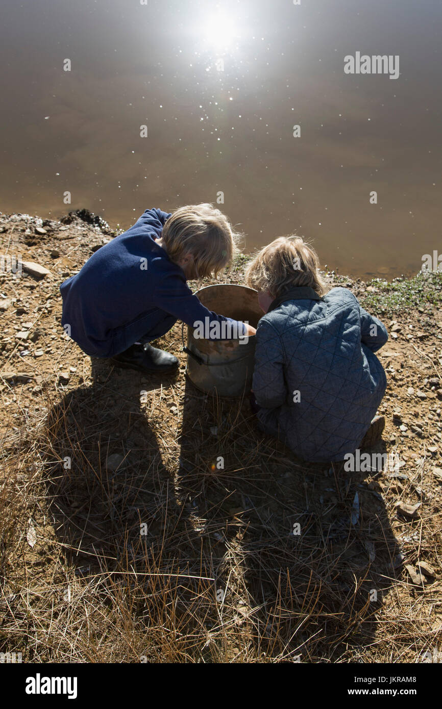 High angle view of boys crouching by bucket at the edge of a river ...