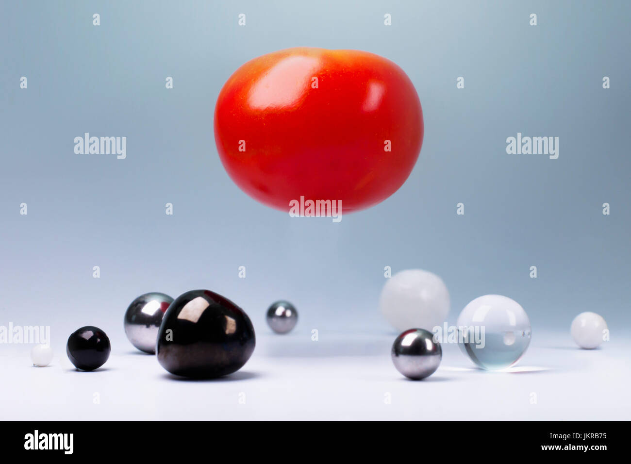 Tomato in mid-air over small round objects below against gray ...