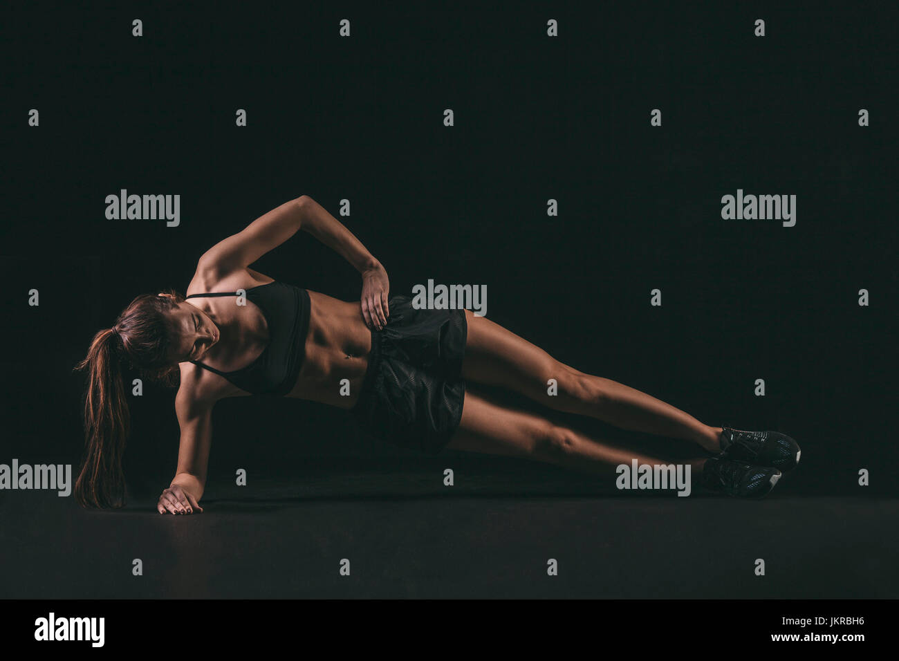 Full length of determined woman doing side plank exercise against black ...