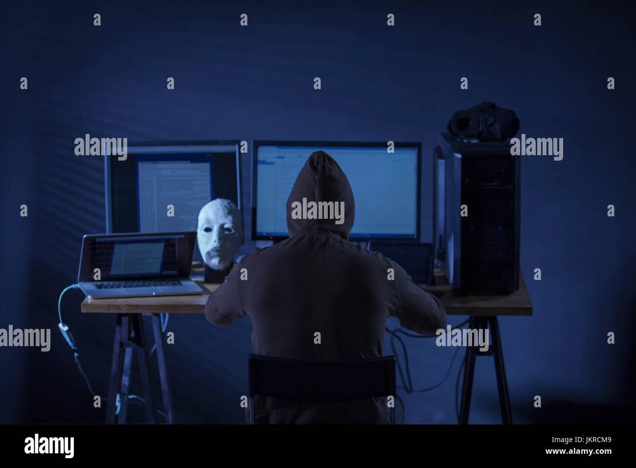 Rear view of computer hacker sitting at desk with equipment against ...