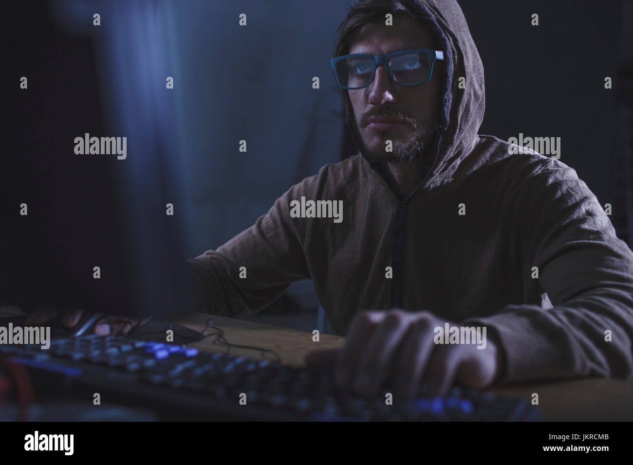 Serious burglar wearing hooded shirt using computer at table Stock ...