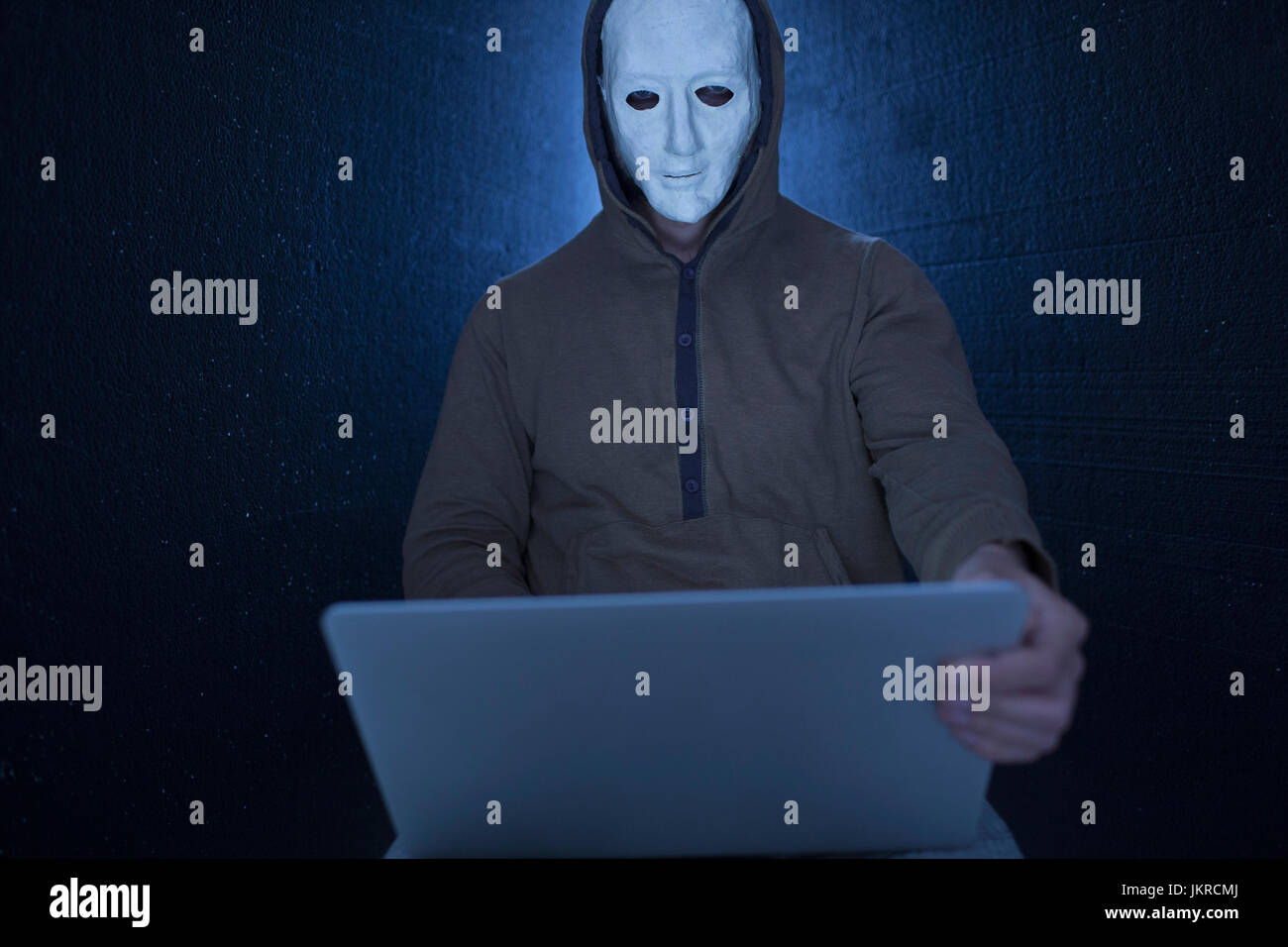 Computer hacker wearing mask using laptop against black background ...