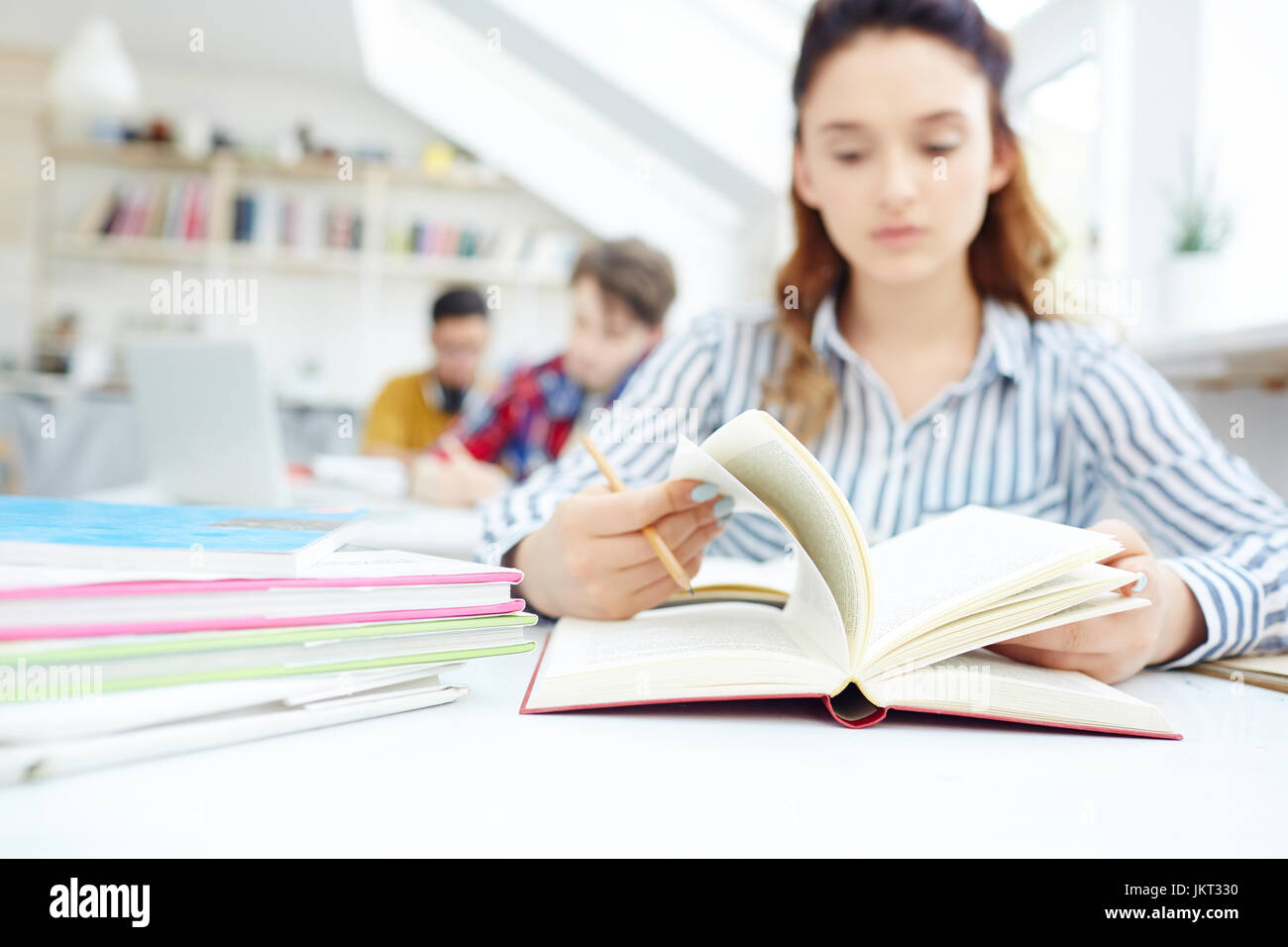 Girl looking through textbook in library Stock Photo - Alamy