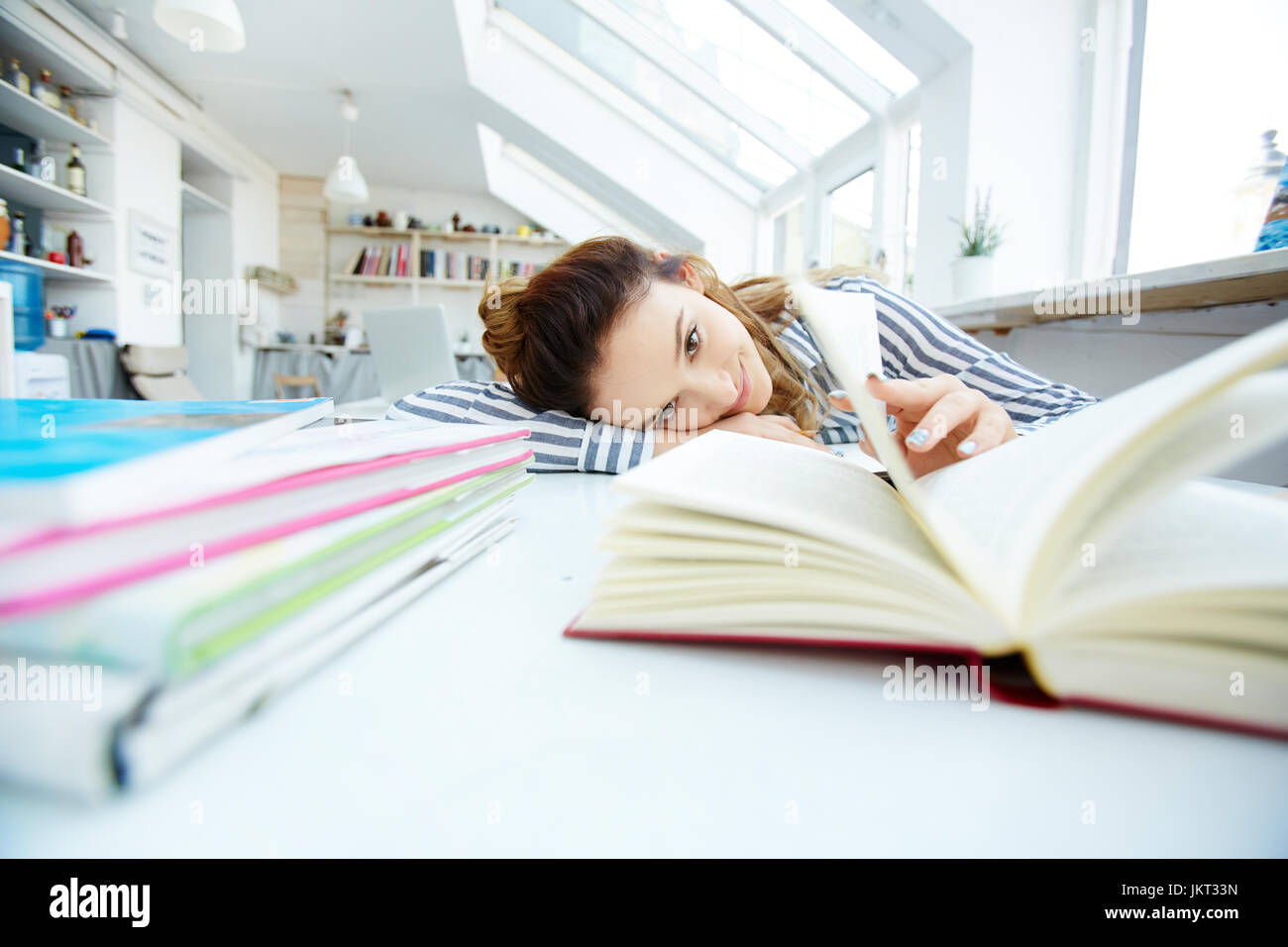 Cute learner lying on desk with open book in front of her face Stock ...