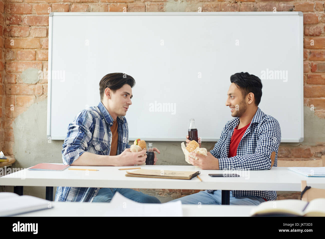 Modern guys with sandwiches and drinks having lunch by desk Stock Photo ...