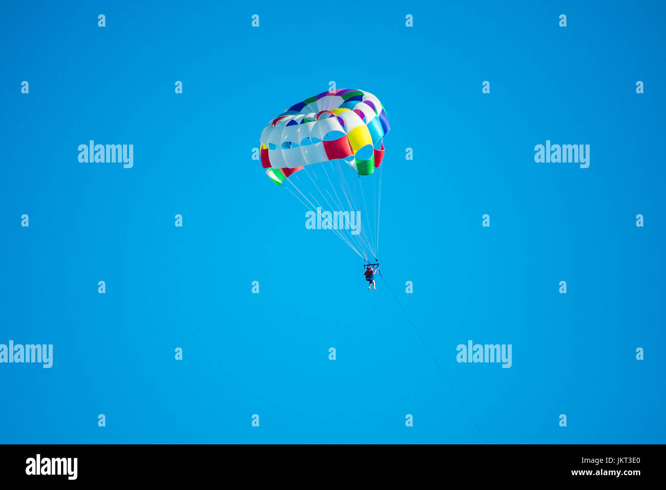 Parasailor on multi-colored parachute flying in blue clear sky, sunny ...