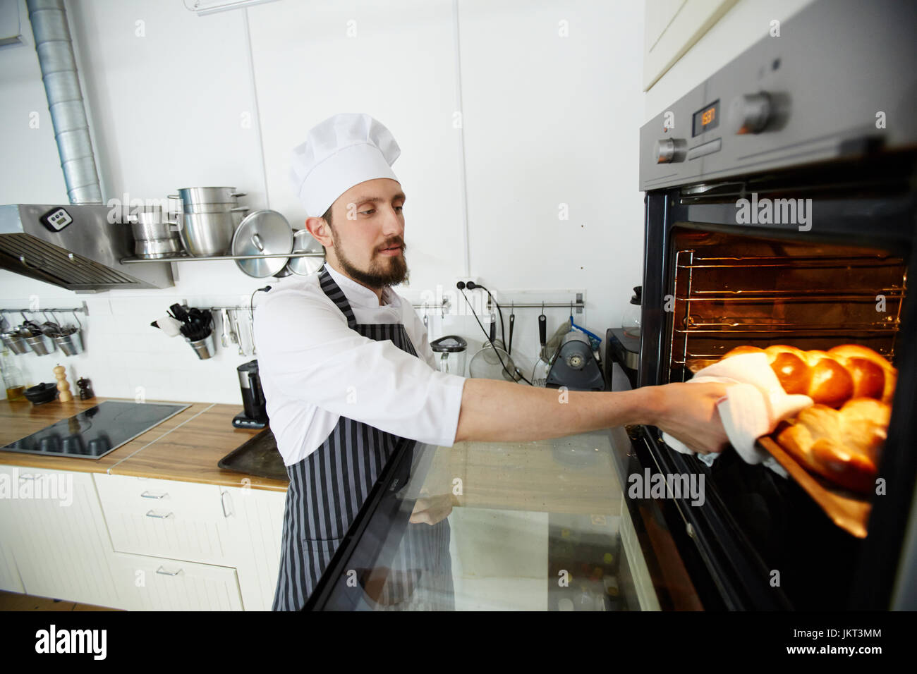 Professional baker taking out hot tray with crusty buns Stock Photo - Alamy