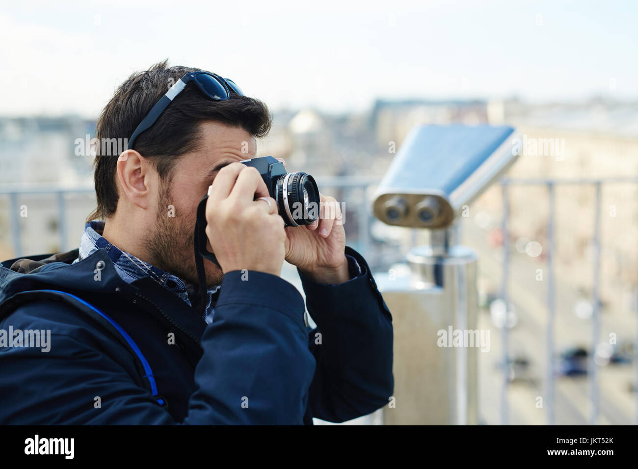 Young man taking picture using photo camera while standing on rooftop ...