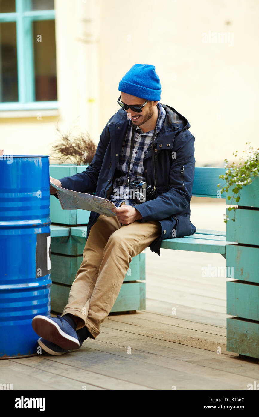 Portrait of modern young man looking up directions in map tourist guide ...