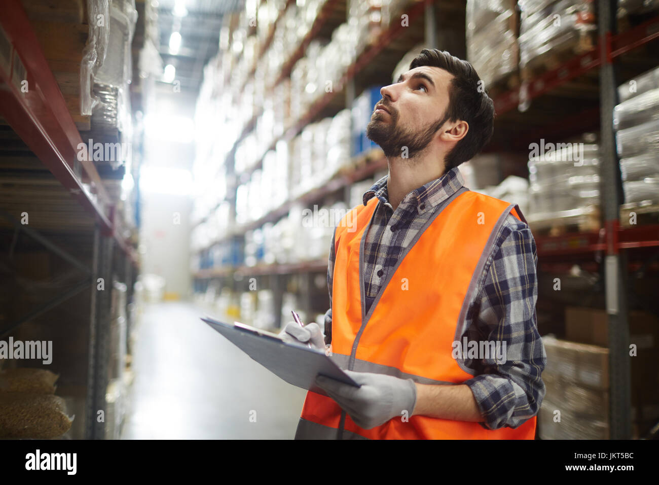 Portrait of warehouse worker looking up the tall shelves doing ...