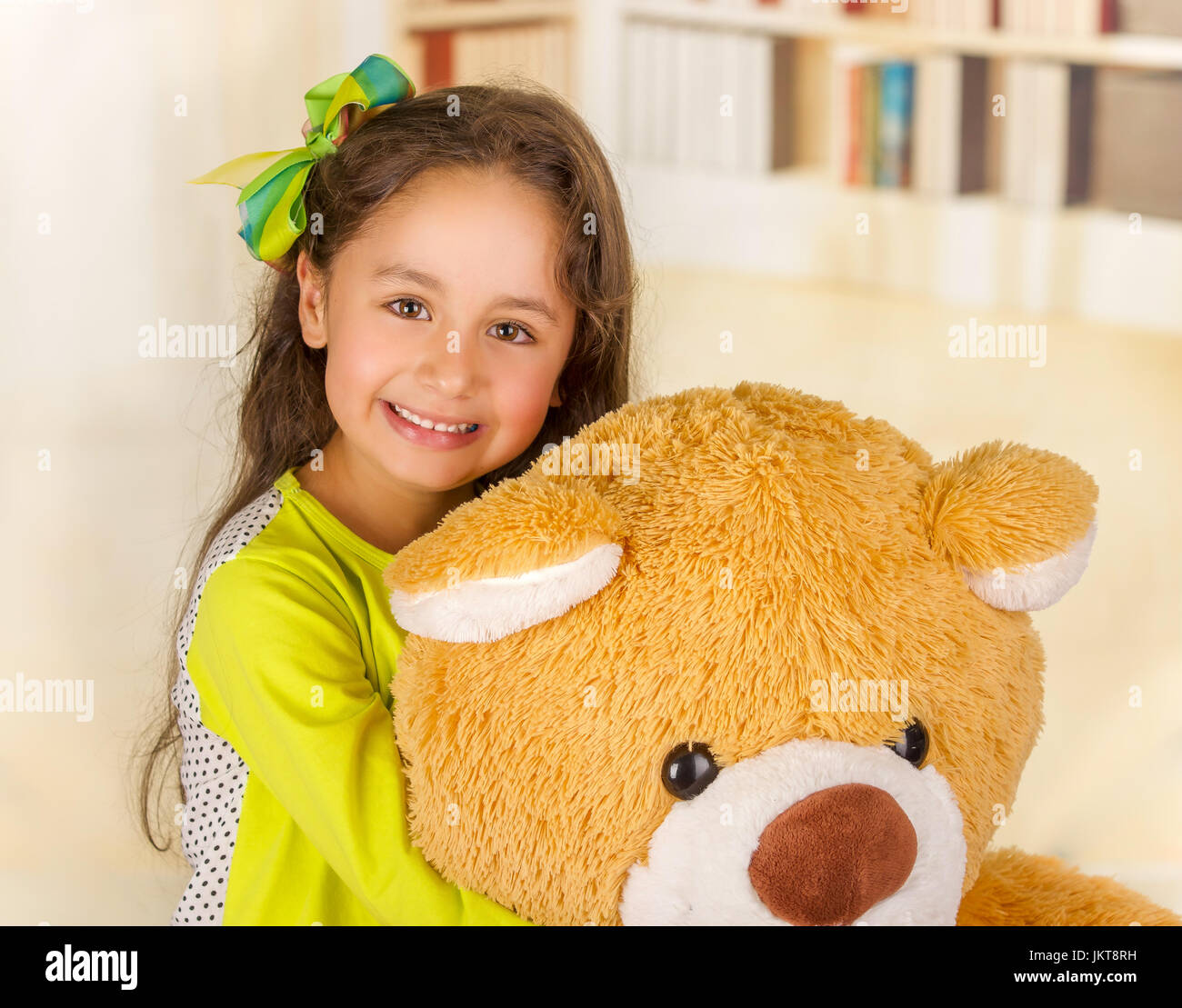 A portrait of a young pretty girl smiling and hugging her teddy bear ...