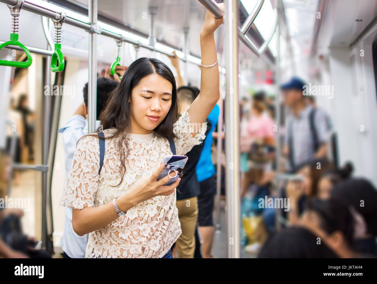 Asian girl using phone on busy subway train Stock Photo - Alamy