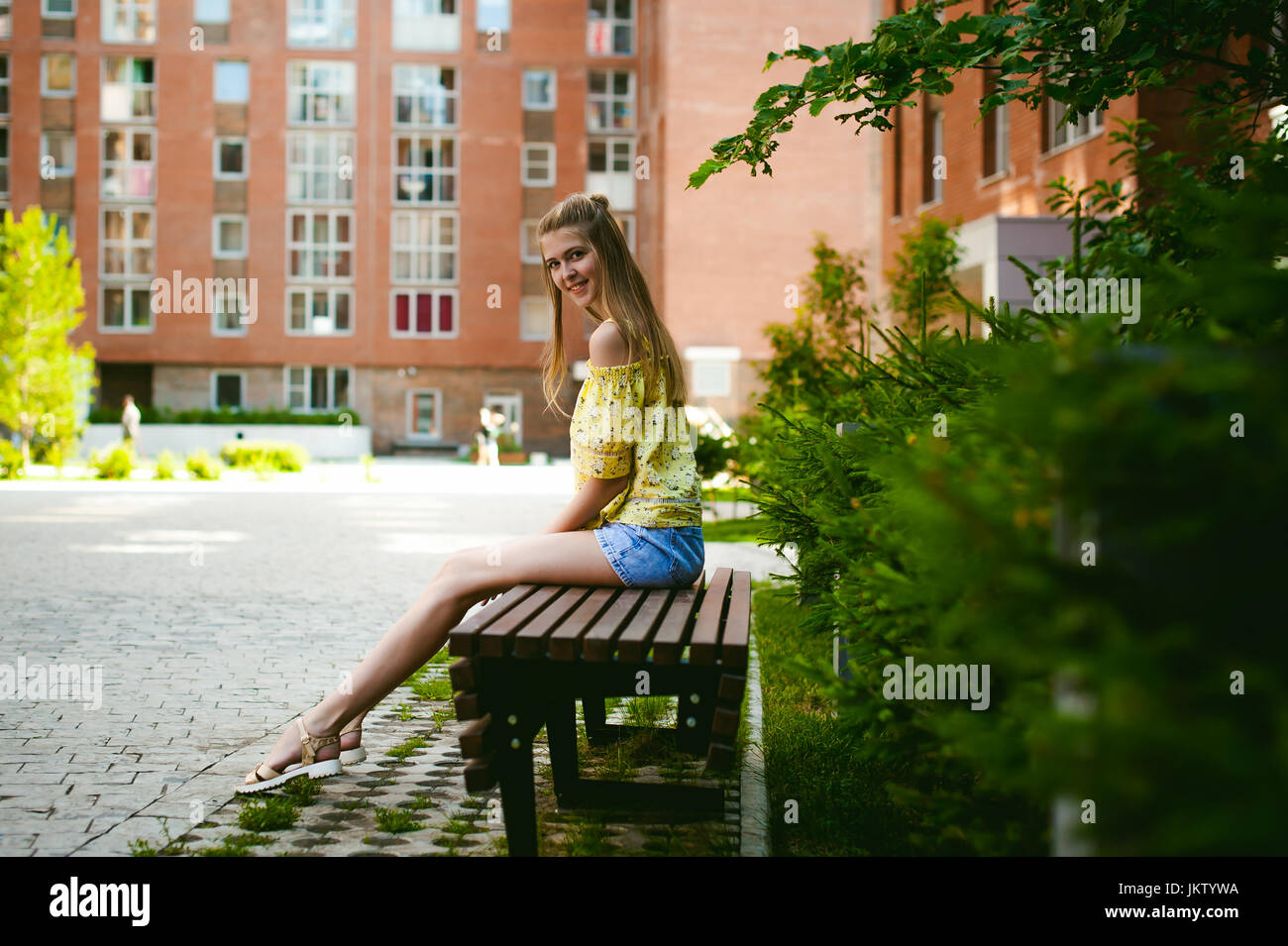 Portrait of a young pretty woman in blue denim jeans shorts sitting on ...