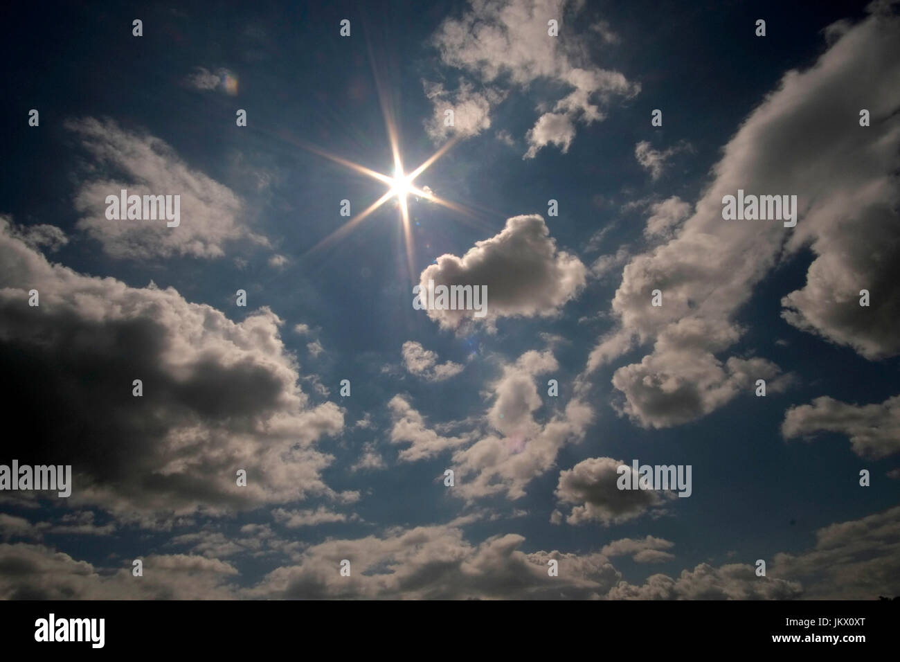 A blue sky with white clouds and a sun starburst Stock Photo - Alamy