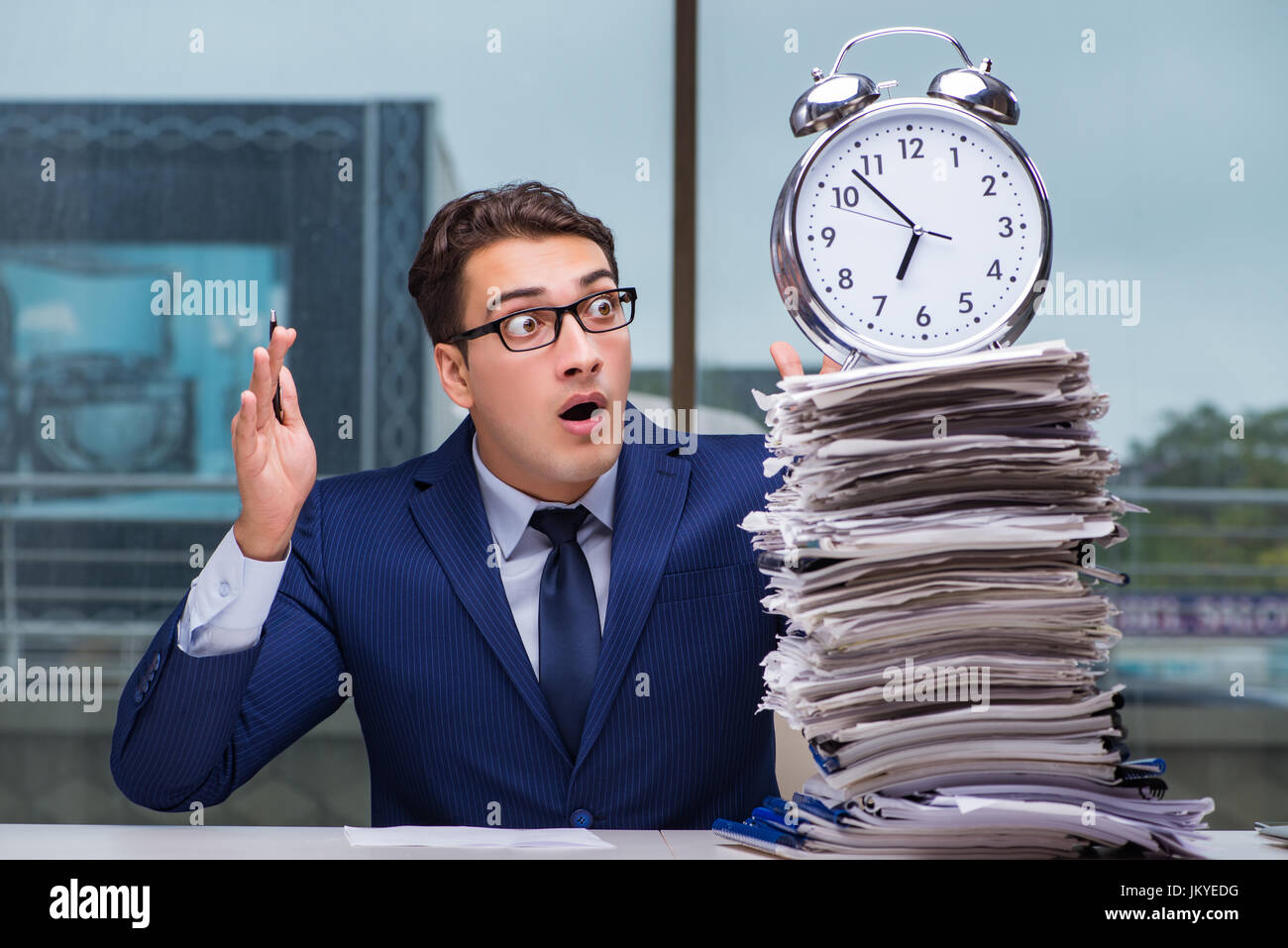 Businessman with pile stack of paper paperwork and an alarm clock ...