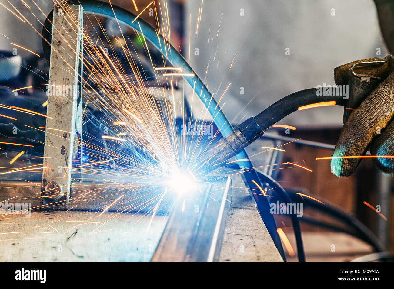 A close-up of welding a metal with a welding machine on a wooden table ...