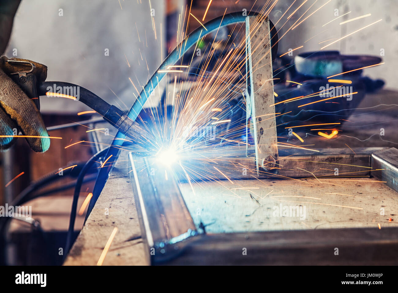 A close-up of welding a metal with a welding machine on a wooden table ...