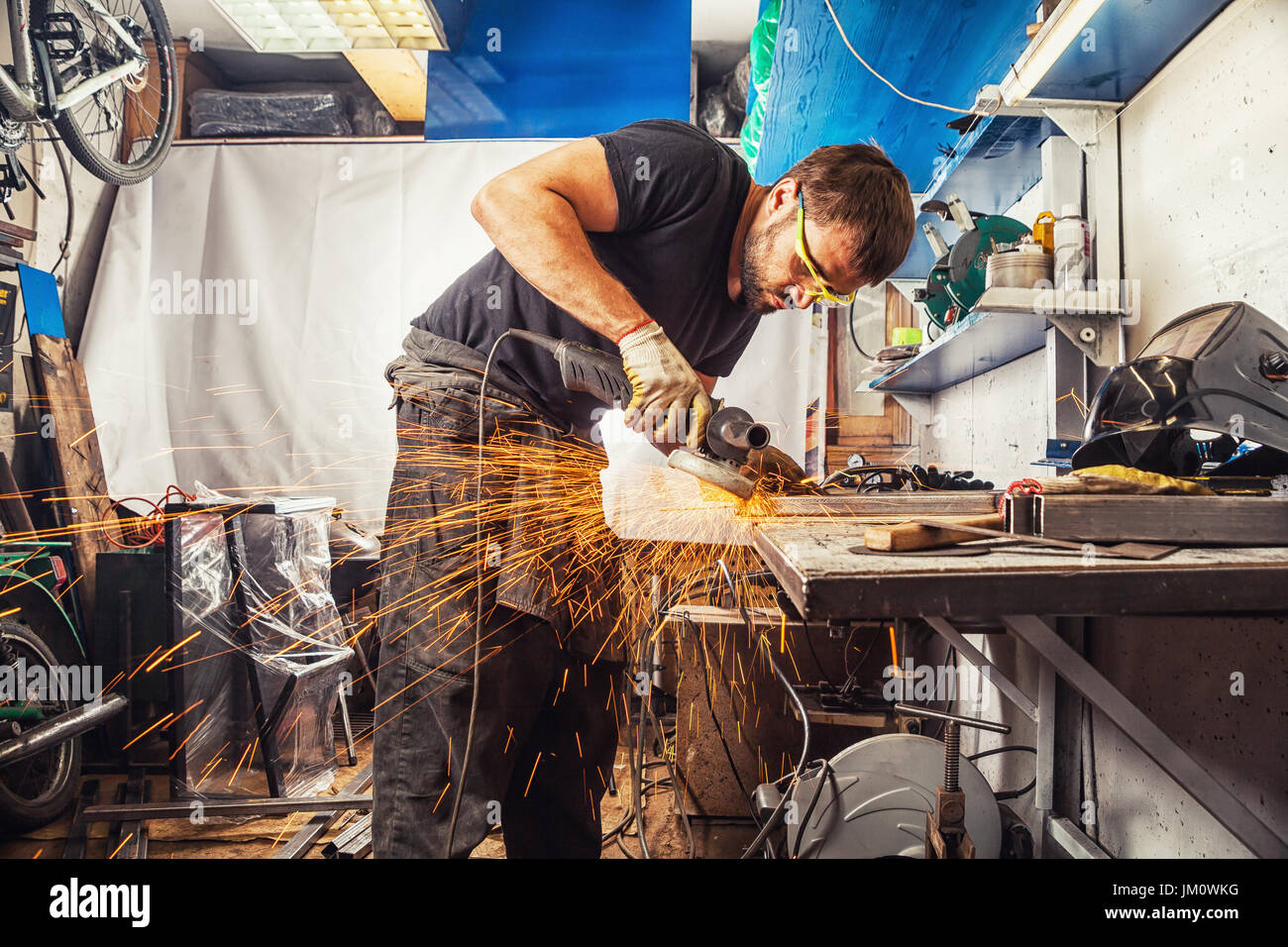 A strong man with hard-working hands in work clothes brewing a metal ...