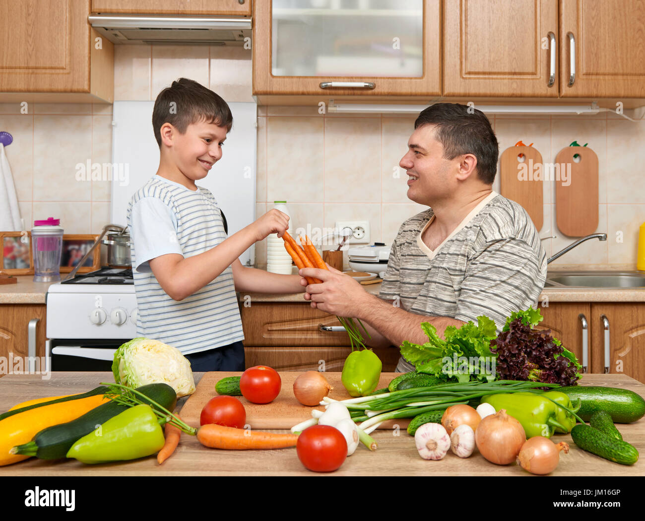Father and son cooking and having fun with vegetables in home kitchen ...